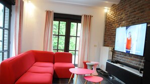 Uma sala de estar moderna com um sofá seccional vermelho, uma televisão de tela plana montada numa parede de tijolos e uma janela grande com cortinas.