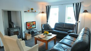 Uma sala de estar com lareira, sofás de couro, televisão e uma mesa de centro com flores.