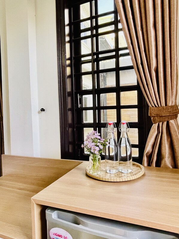 Uma mesa de madeira com uma bandeja trançada que contém duas garrafas e um vaso de flores.