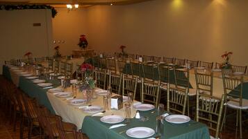 Uma sala de banquetes com mesas compridas preparadas para refeições, cadeiras alinhadas em fileiras e arranjos florais em cada mesa.