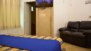 Quarto de hotel com uma cama, uma televisão presa à parede e um sofá de couro marrom.