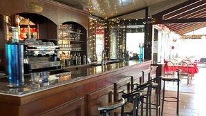 Uma área de bar com balcão de madeira, banquetas e prateleiras com garrafas.