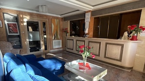 Uma sala de estar moderna com um sofá azul, uma mesa de centro de vidro com flores vermelhas e uma área de cozinha com armários de madeira.