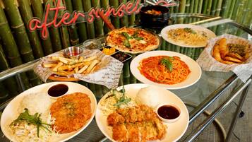 Uma mesa com diversos pratos, incluindo fritos, massa e pizza, com um fundo de bambu e um letreiro neon.