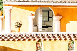 Fachada amarela vibrante com telhado ladrilhado e porta de entrada para uma área de cozinha.