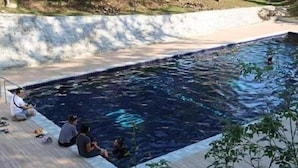Piscina com pessoas sentadas e relaxando no deck.