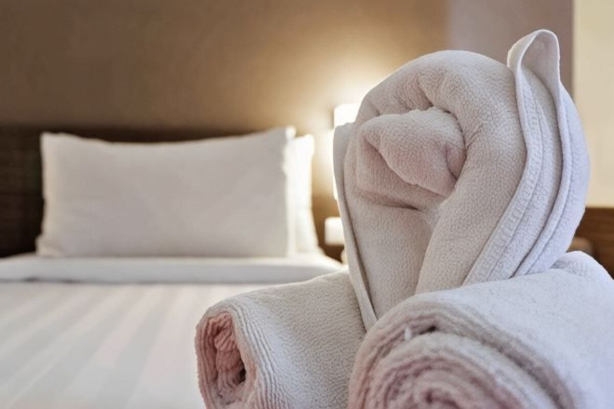 Cama bem arrumada com roupa branca e uma toalha enrolada ao lado.