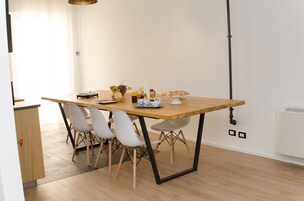 Uma área de refeições moderna com uma mesa de madeira, cadeiras brancas e diversos alimentos e bebidas.