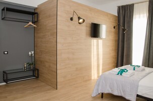 Quarto de hotel moderno com parede de destaque em madeira, cama com toalhas brancas dobradas e uma televisão montada, além de luminária pendente.