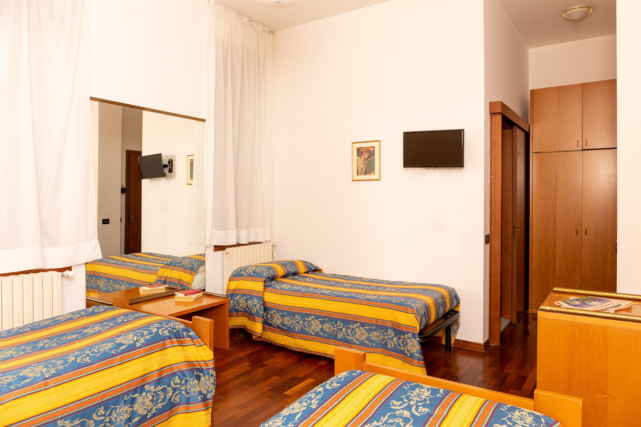 Quarto com três camas, um guarda-roupa de madeira, uma TV de tela plana e um quadro na parede.