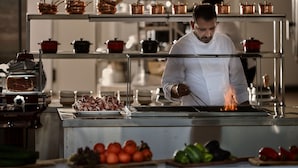 Um chefe de cozinha cozinhando com chama em uma churrasqueira em uma cozinha profissional.