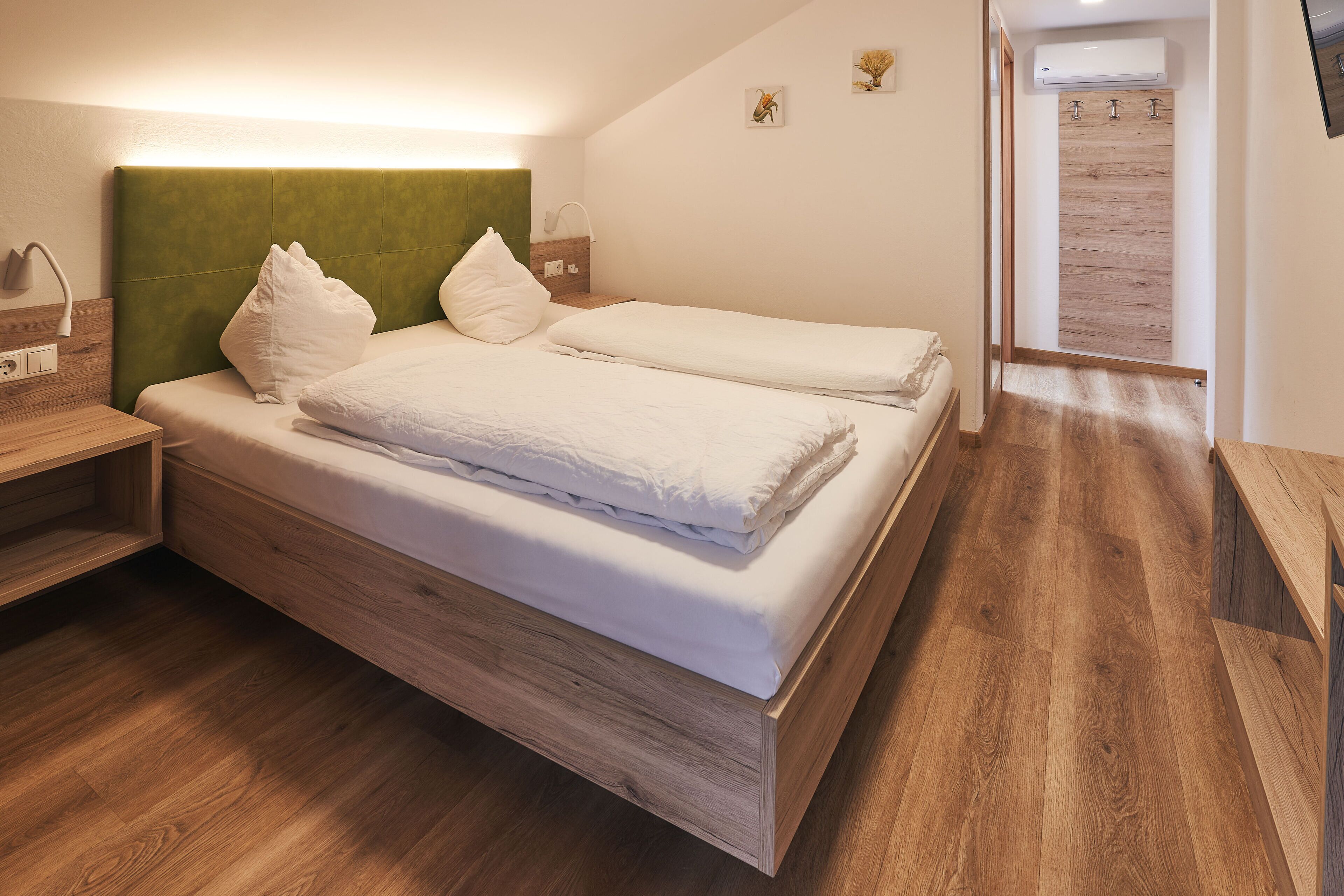 Uma cama de casal com cabeceira verde, mesas de cabeceira de madeira e uma mesa de apoio com abajur.