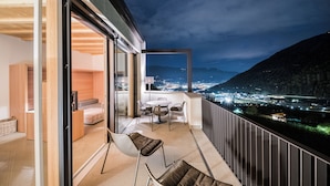 Varanda com vista para a cidade à noite, área de refeições e quarto com portas de vidro deslizantes.