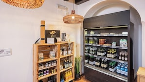 Loja com prateleiras cheias de bebidas diversas, uma luminária de vime pendurada e um expositor de madeira com garrafas.