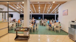 Uma sala de jantar com mesas, cadeiras, um display de vinhos e vista para o exterior à noite.