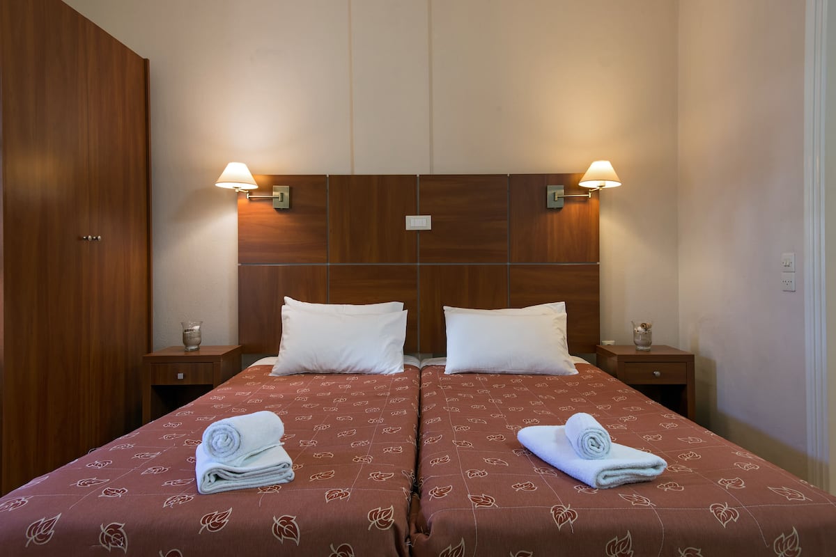 Quarto duplo com duas camas, cada uma com cabeceira de madeira, mesas de cabeceira com abajures e toalhas dobradas com cuidado.