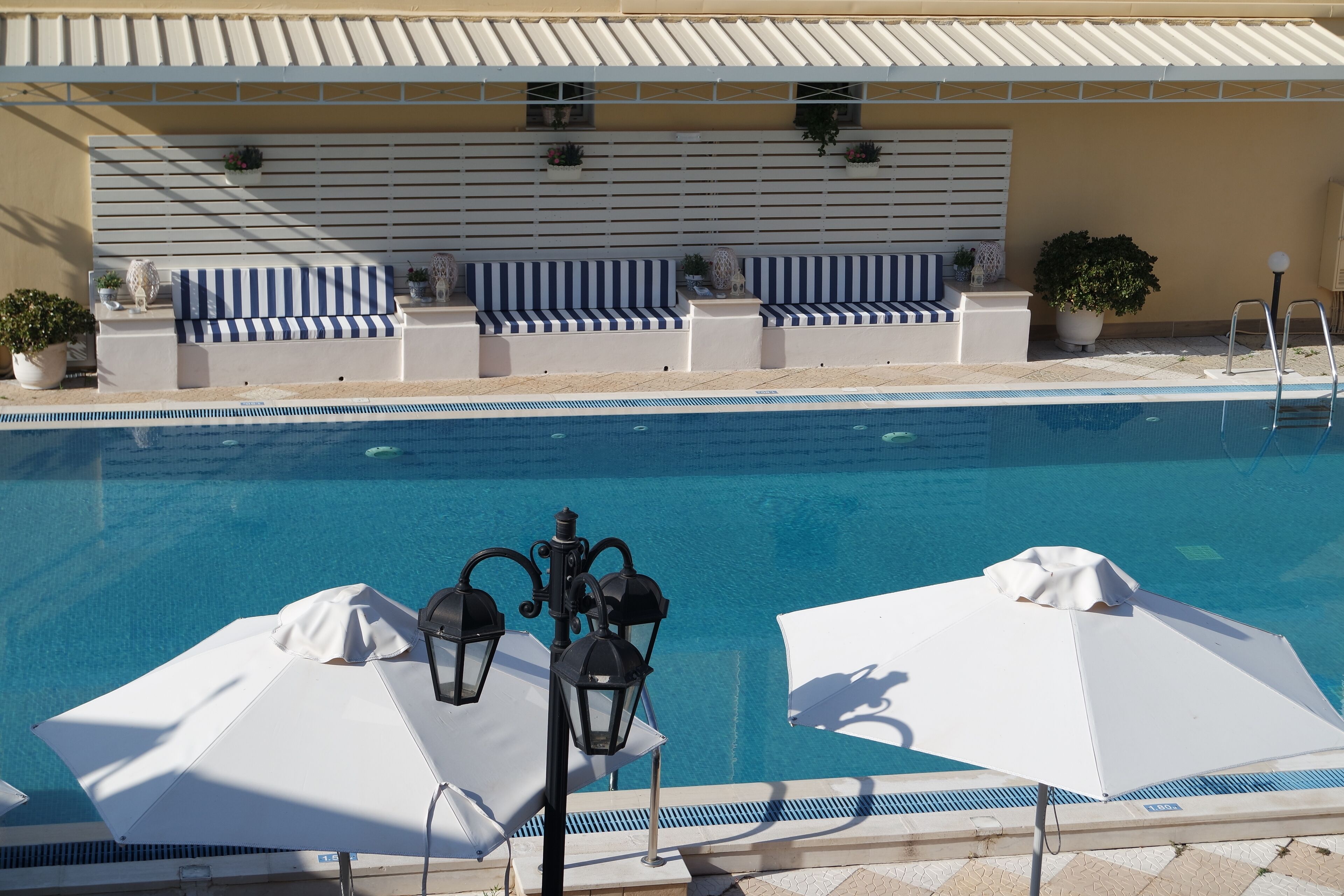 Área da piscina com guarda-sóis brancos, espreguiçadeiras e um espaço de estar coberto.
