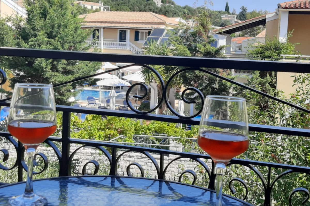 Uma varanda com duas taças de vinho, com vista para uma piscina e uma colina com edifícios.