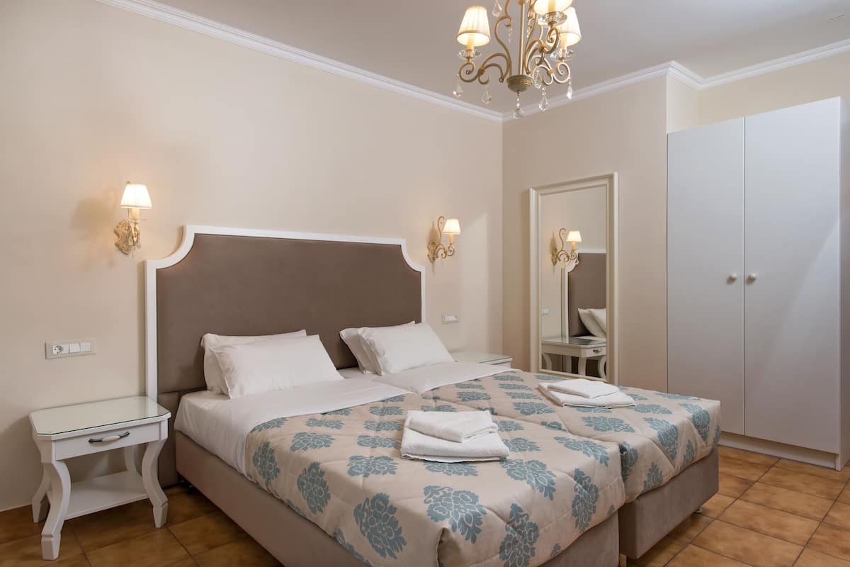 Quarto de hotel com cama de casal, mesas de cabeceira, guarda-roupa e um candelabro.