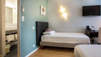 Quarto de hotel com duas camas, banheiro com espelho e TV fixada na parede.