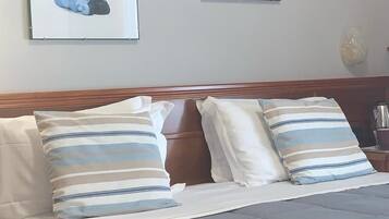 Quarto de hotel com cama, duas almofadas, mesa de cabeceira e duas obras de arte emolduradas na parede.