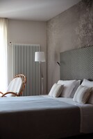 Quarto de hotel com cama, poltrona, abajur e radiador.