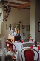 Uma área de refeições com mesas preparadas para quatro pessoas, cadeiras de madeira e toalha de mesa branca.