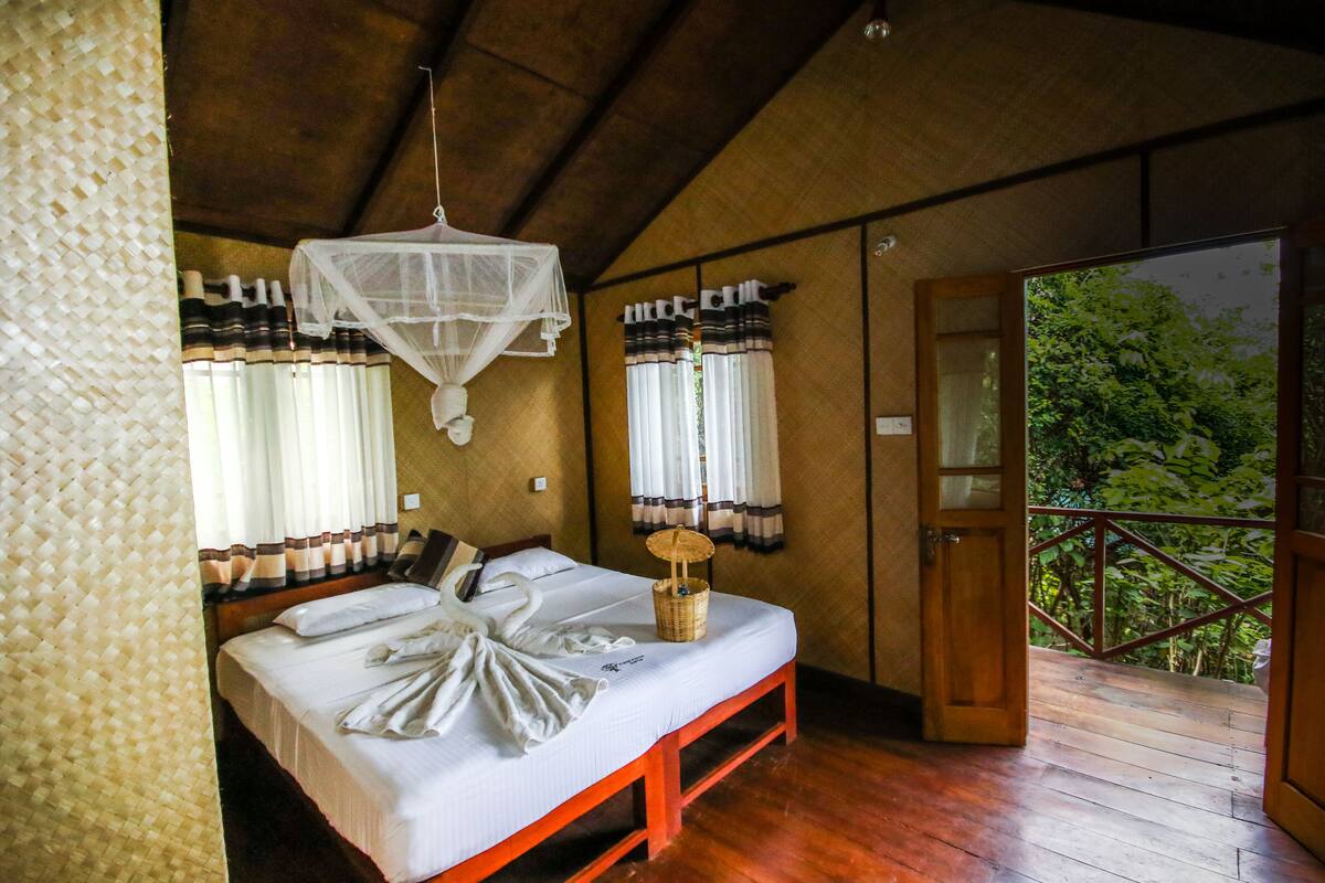 Quarto com cama, mosquiteiro e varanda com vista para árvores.
