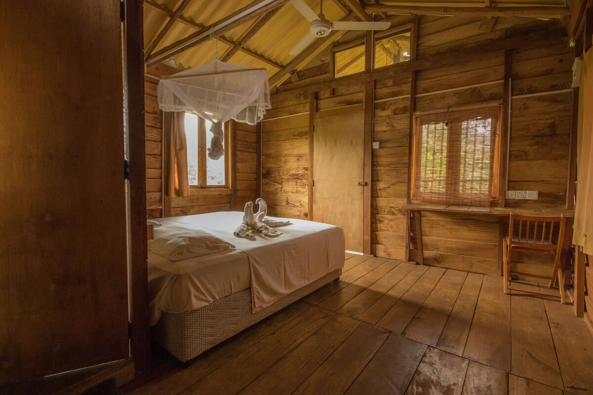 Quarto de cabana de madeira com uma cama, uma mesa e uma cadeira.