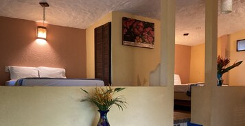 Quarto de hotel com uma cama, uma luminária na parede, um quadro e um vaso com plantas.