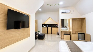 Quarto de hotel moderno com TV de tela plana, cozinha compacta, cama e um pequeno refrigerador.