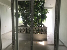 Um corredor com divisória de vidro, um banco de concreto e escadas que levam a uma varanda com vegetação.