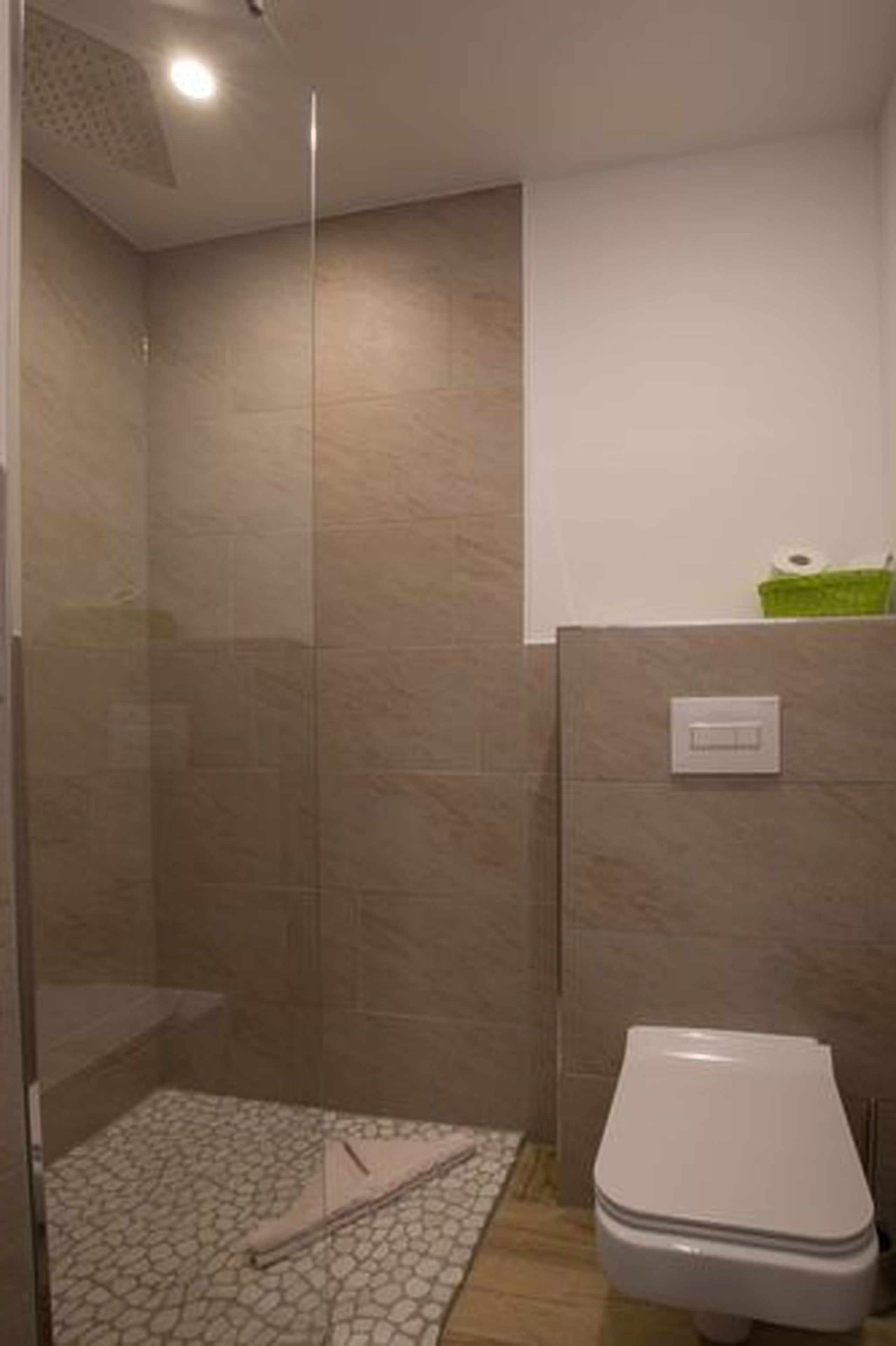 Casa de banho com chuveiro, sanita e chão em mosaico.