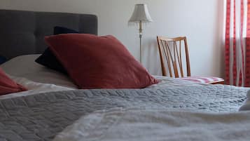 Cama bem arrumada com almofadas, abajur, uma cadeira e um quadro na parede.