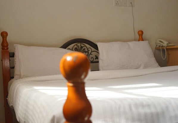 Cama com roupa de cama branca e cabeceira de madeira.