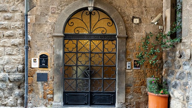 Um edifício histórico de pedra com um portão de metal decorativo com a inscrição 'ISTITUTO SS SALVATORE'.