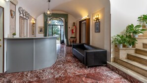 Um corredor espaçoso com teto curvo, sofá de couro preto, piso de mármore e escada decorada com plantas em vasos.