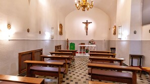Interior de igreja com bancos de madeira, um crucifixo, um candelabro e piso xadrez.