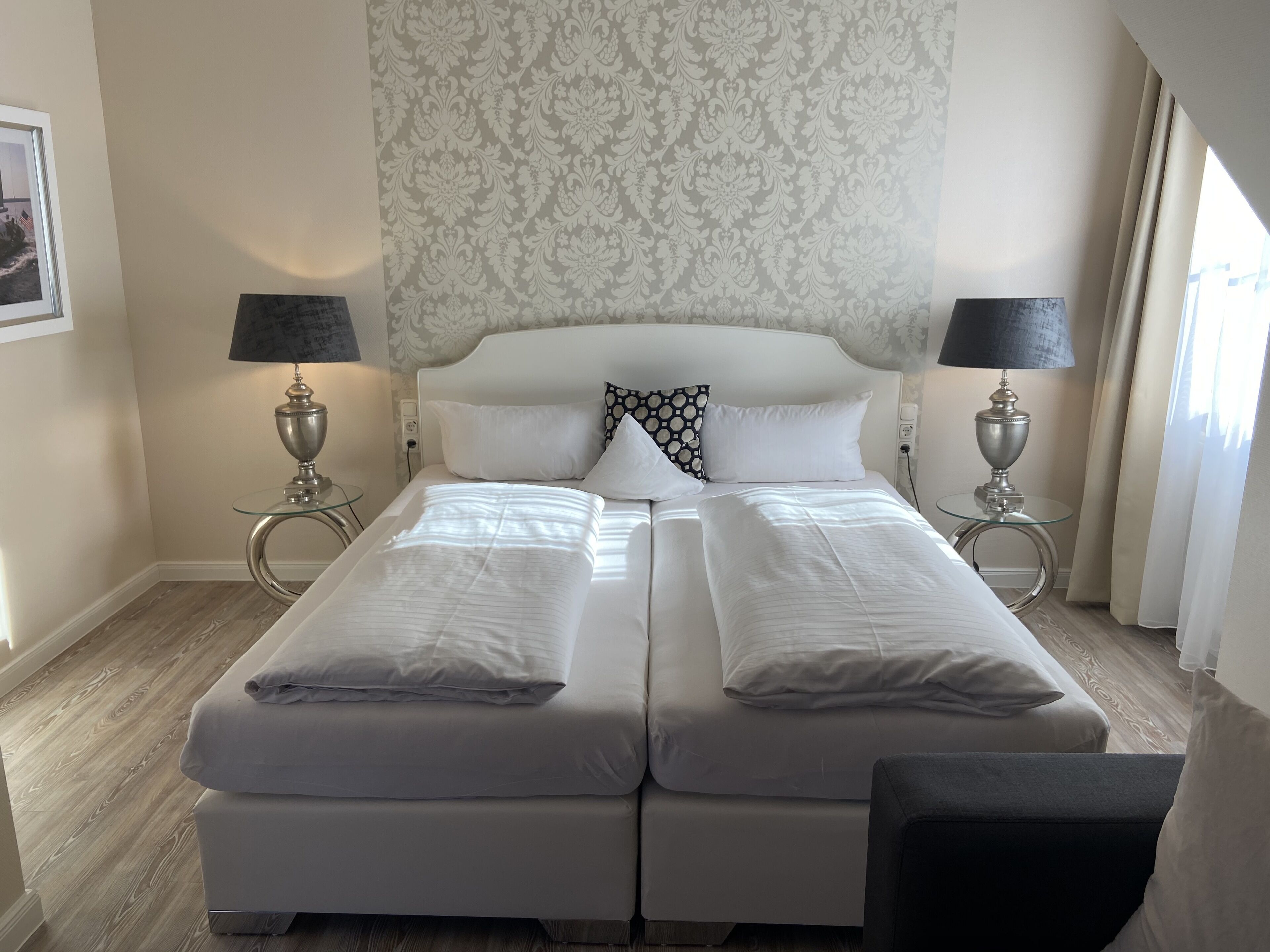Uma cama de casal com duas almofadas, uma mesa de cabeceira com abajur e um papel de parede estampado acima da cama.