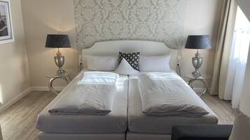 Uma cama de casal com duas almofadas, uma mesa de cabeceira com abajur e um papel de parede estampado acima da cama.