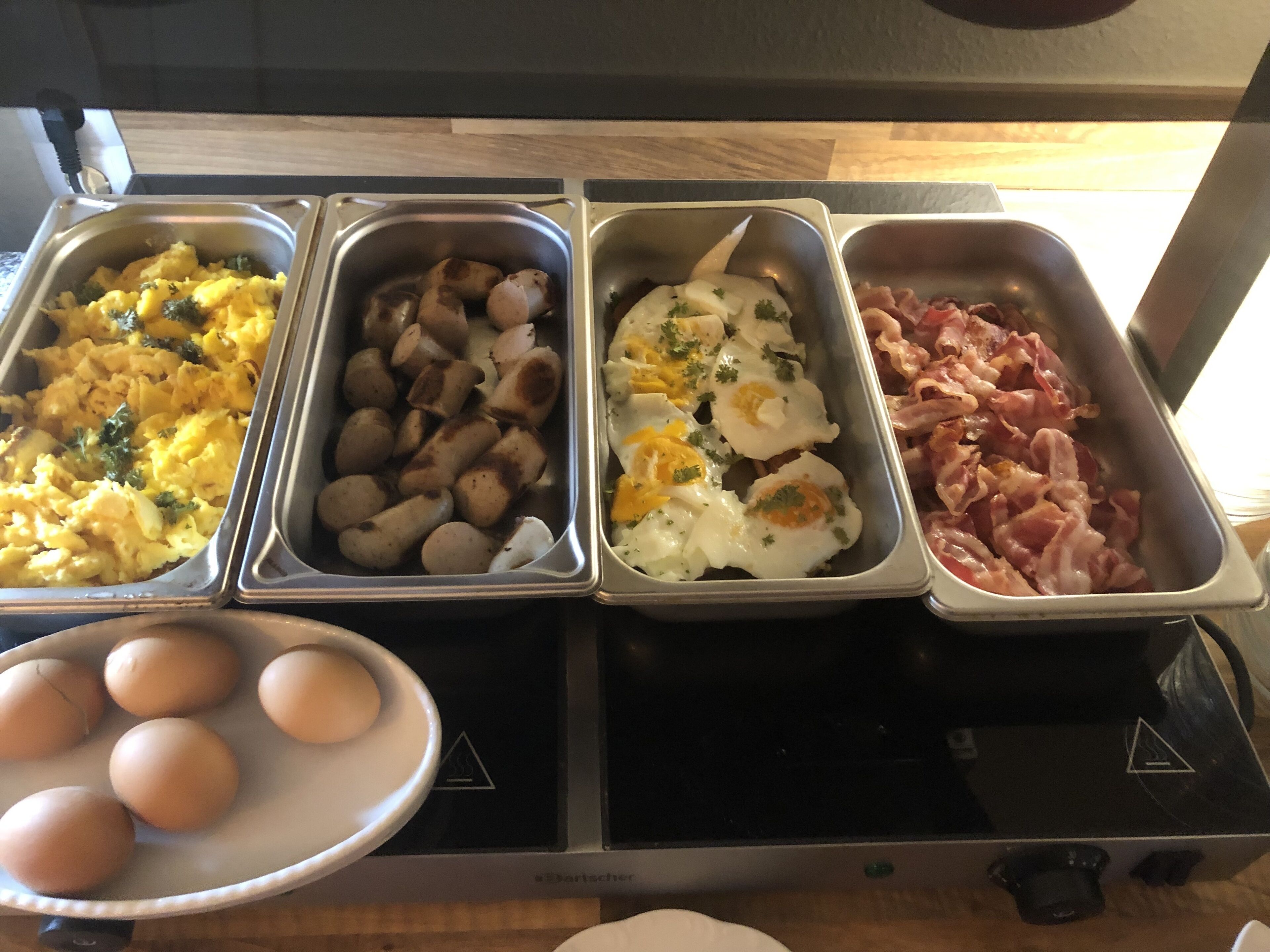 Buffet com ovos mexidos, salsichas, ovos fritos e bacon.