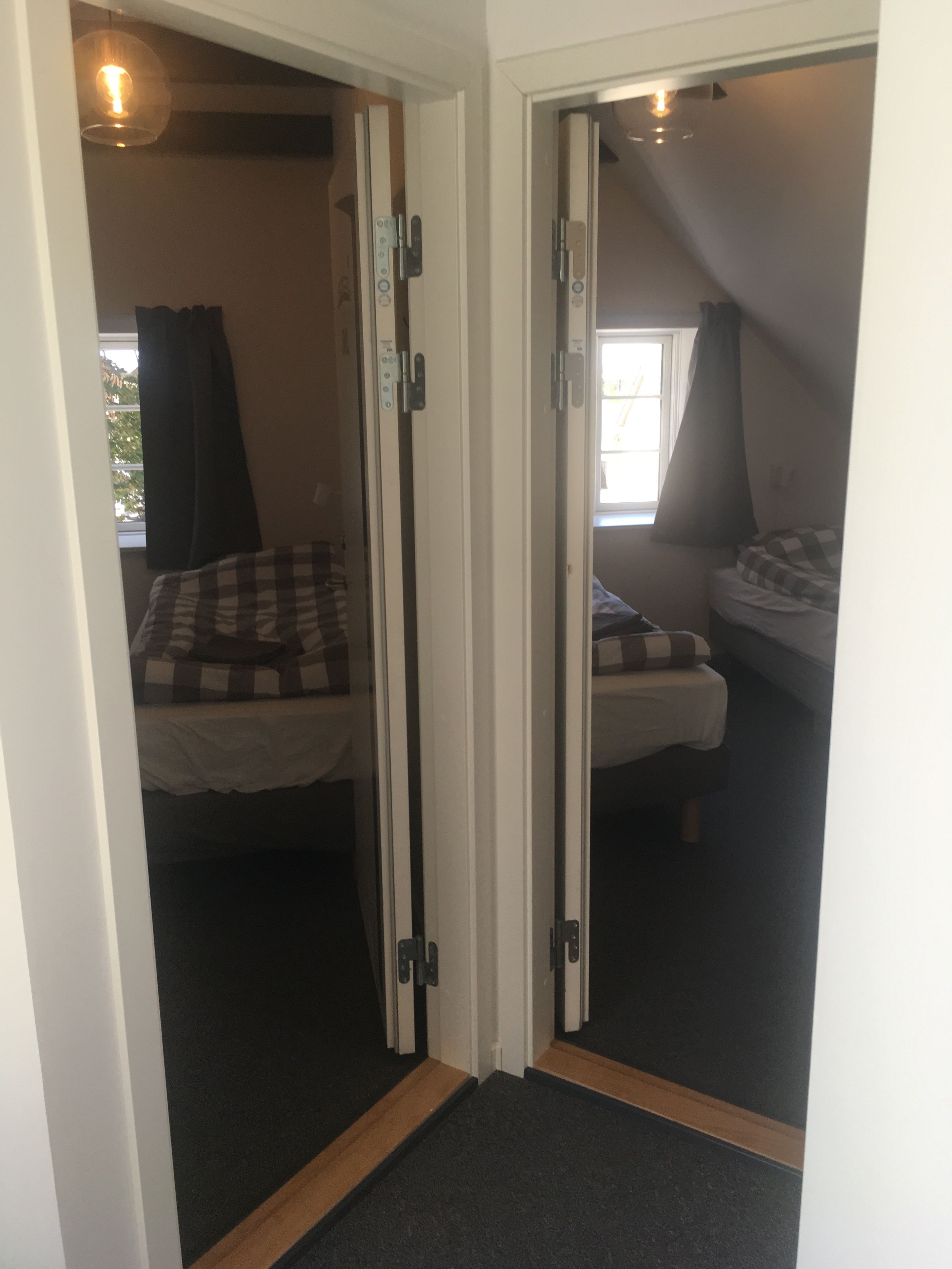 Quarto com cama, janela com cortinas e porta que dá para outro espaço.