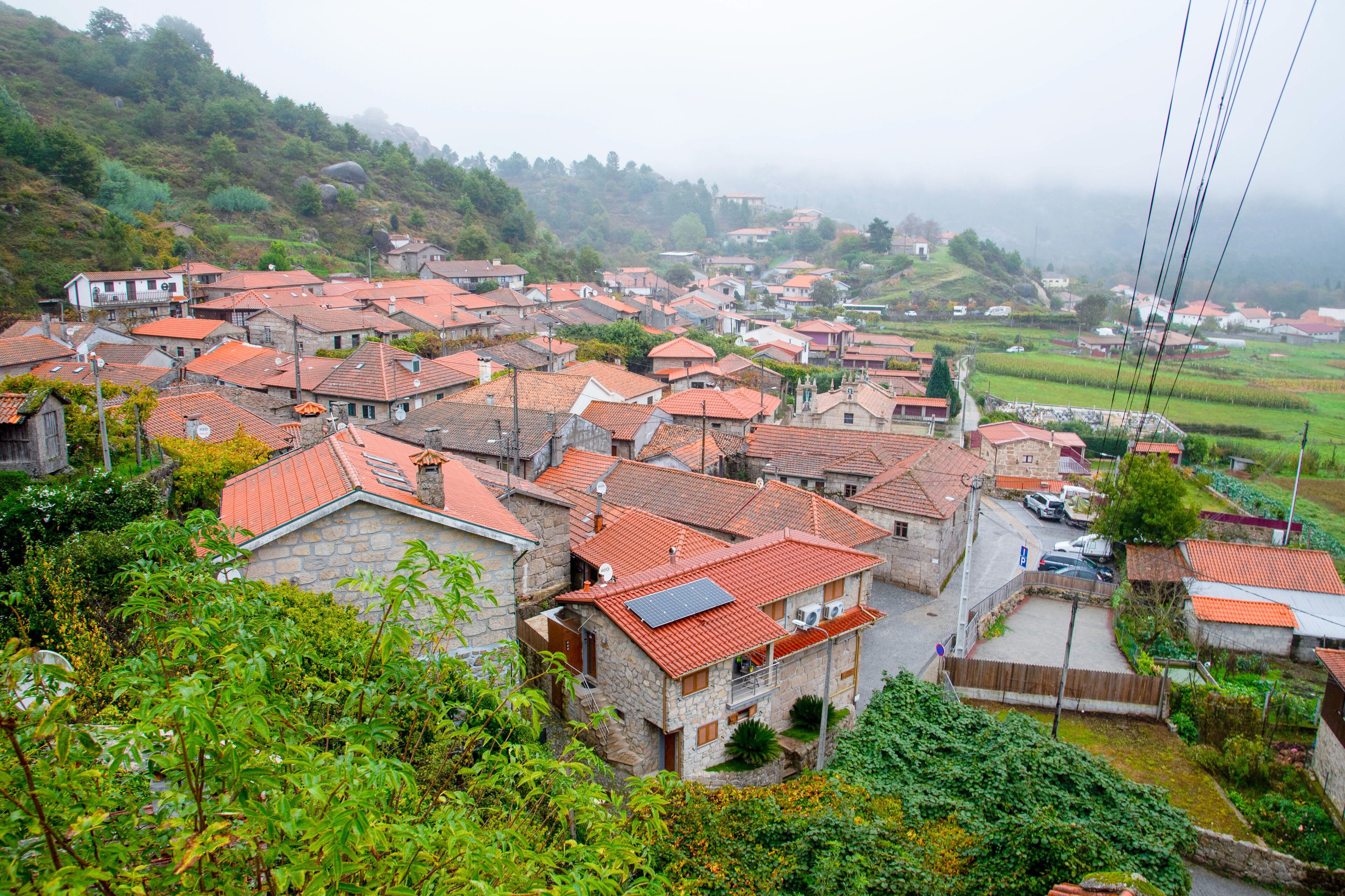 Uma vila numa encosta, com edifícios de pedra tradicionais e telhados de telha vermelha.