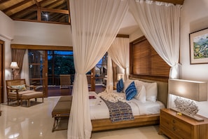 Quarto com cama de dossel, mesa de cabeceira de madeira e vista para o exterior.