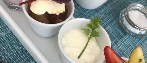 Uma bandeja com um smoothie rosa, uma taça de sorvete com um enfeite de folha, uma pequena tigela de creme e uma tigela com frutas variadas.