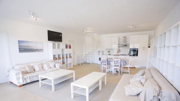 Uma sala de estar moderna, decorada em tons de branco, com sofá, mesa de centro e um espaço de jantar com cadeiras e mesa.