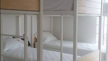 Quarto com beliches, painéis de madeira e roupa de cama branca.