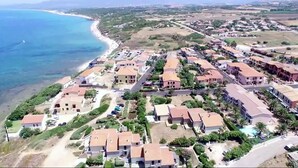 Vista aérea de uma área residencial costeira, com casas, uma praia e céu claro.