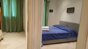 Quarto com cama, cortinas verdes, quadro pendurado na parede e piso de azulejos.