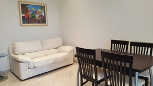 Um sofá branco, uma mesa de jantar de madeira com quatro cadeiras e um quadro pendurado na parede.